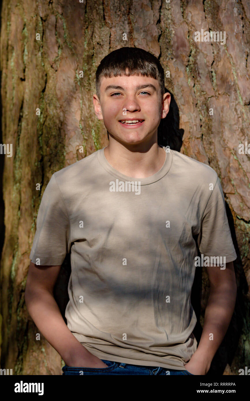 Portrait of a caucasian teenage boy leaning against a tree on a warm ...