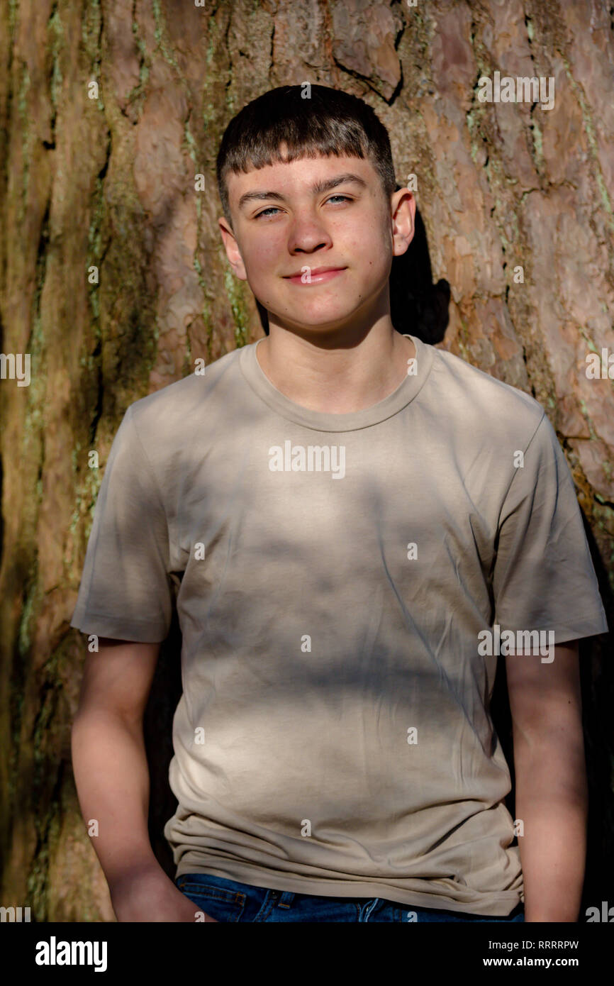Portrait of a caucasian teenage boy leaning against a tree on a warm ...