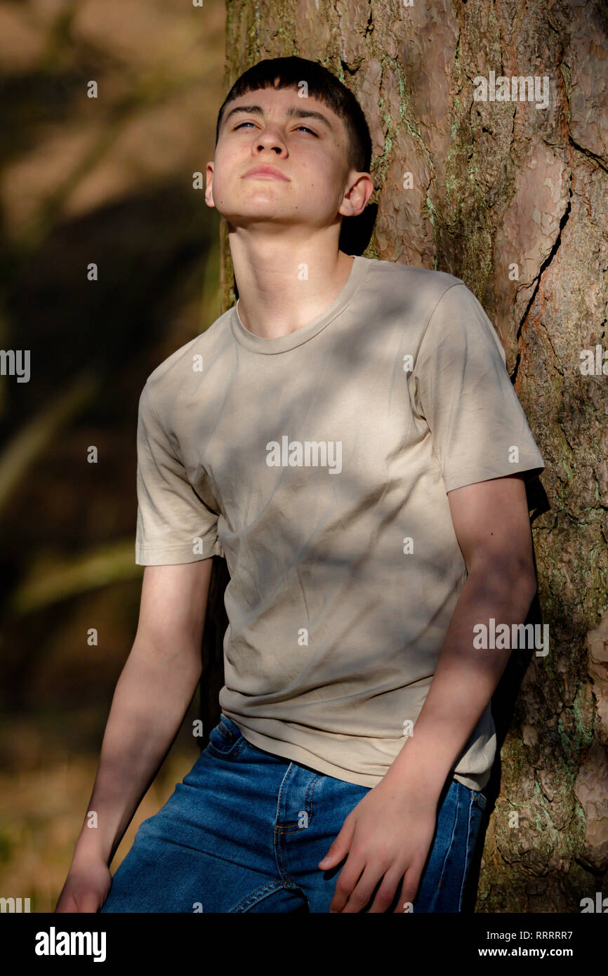 Portrait of a caucasian teenage boy leaning against a tree enjoying the ...