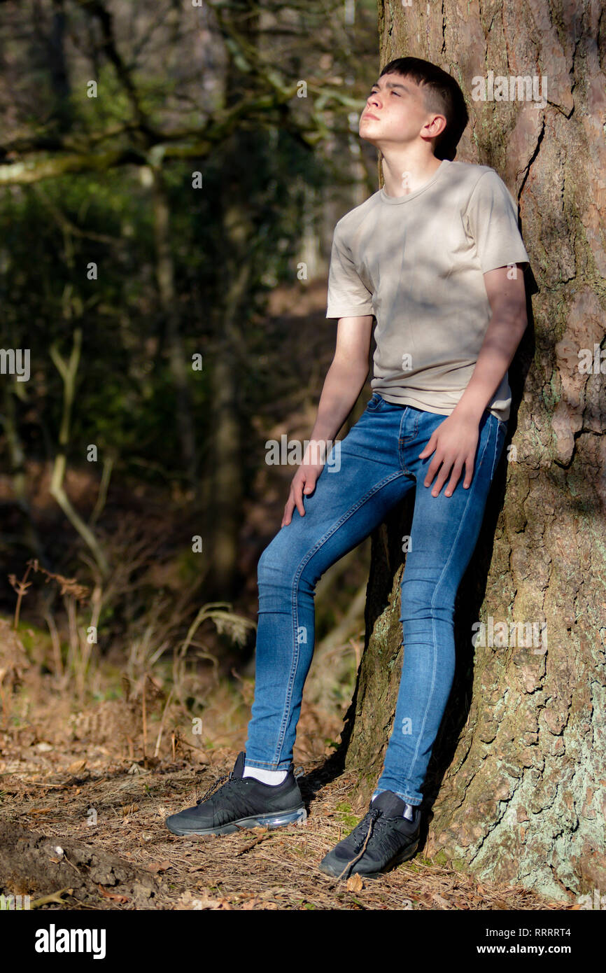 Portrait of a caucasian teenage boy leaning against a tree enjoying the ...
