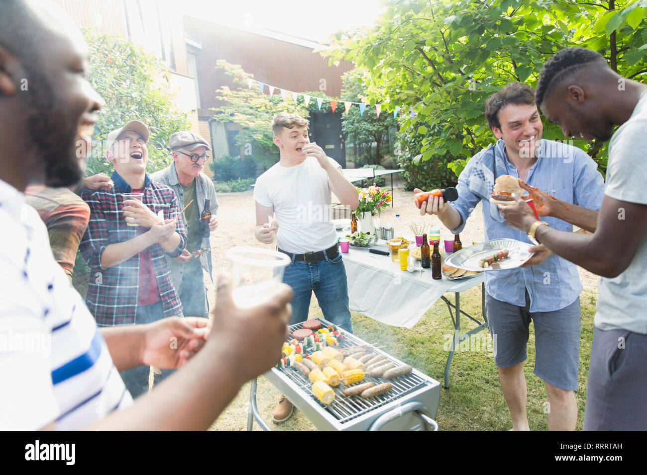 Male friends laughing and eating around barbecue grill in backyard ...