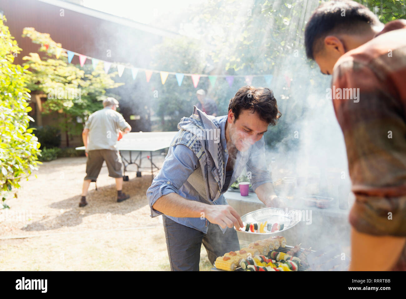 Male friends barbecuing in sunny backyard Stock Photo - Alamy