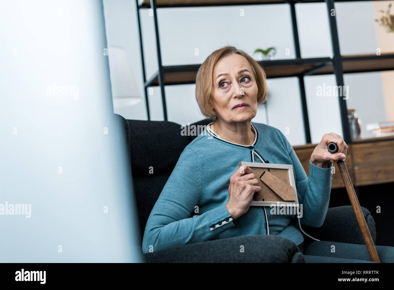 upset senior woman sitting with walking stick and holding picture frame ...