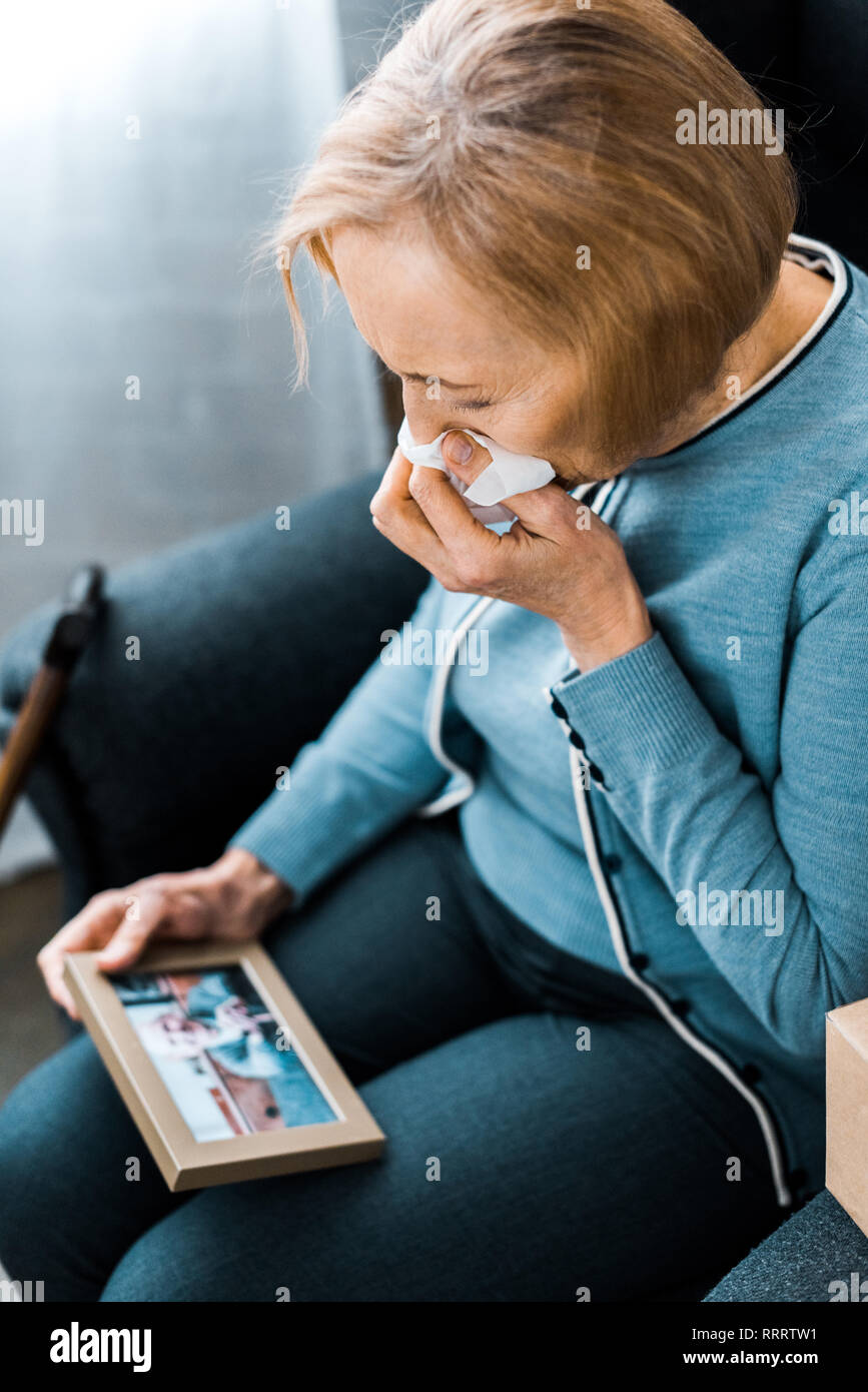 sad senior woman sitting and crying while looking at picture frame ...