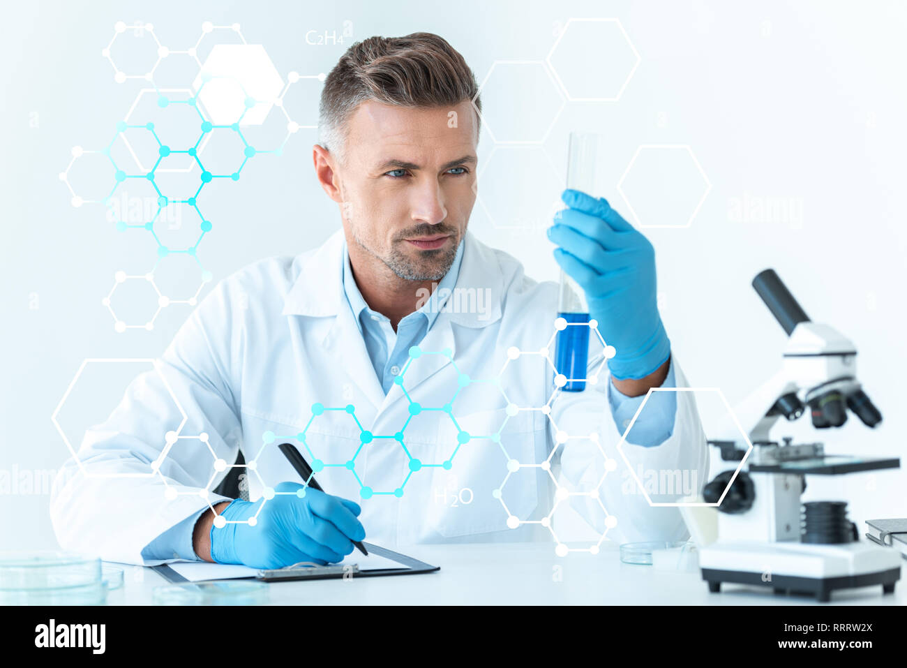 handsome scientist looking at test tube with blue reagent isolated on ...
