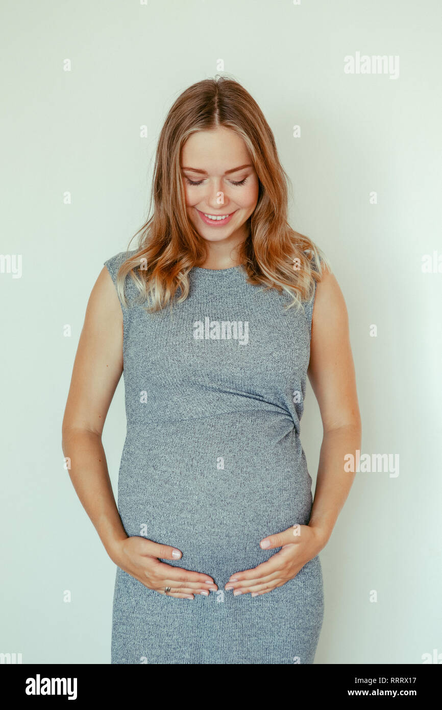Portrait Of Smiling White Caucasian Blonde Pregnant Woman In Grey Dress