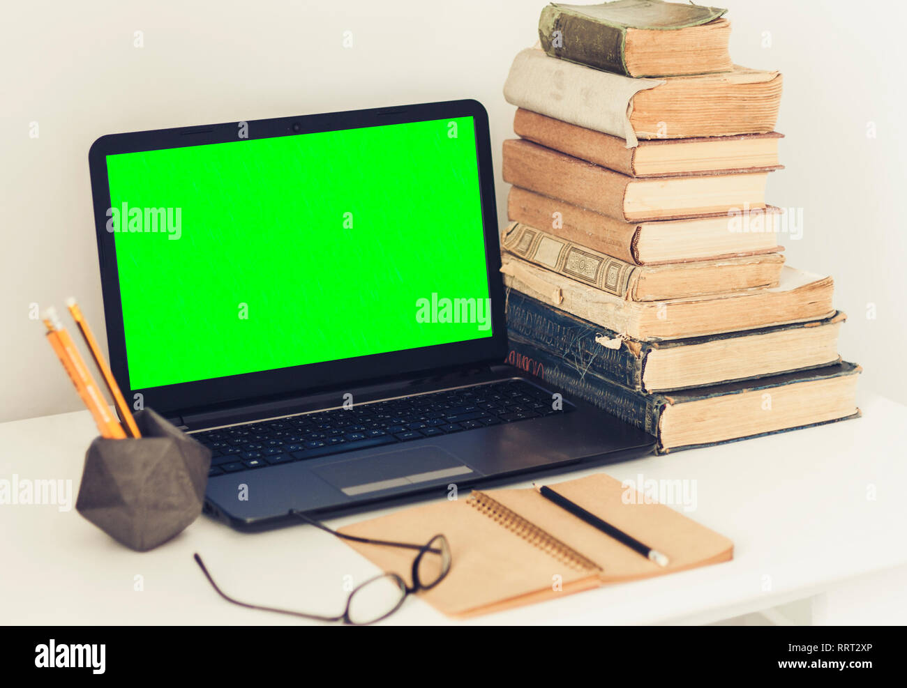 Green screen laptop, stack of old books, notebook and pencils on white ...
