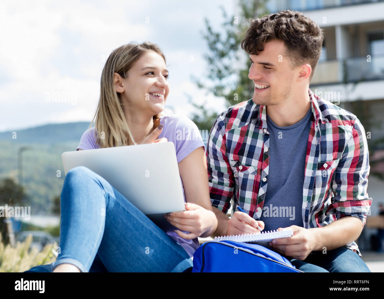 Laughing german student couple with computer outdoor on campus of ...