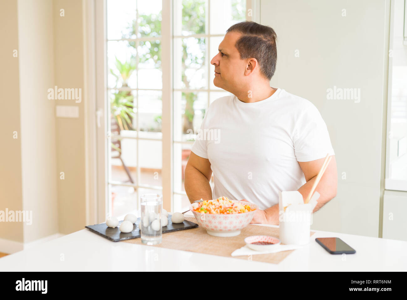 Middle age man eating asian food with chopsticks at home looking to ...