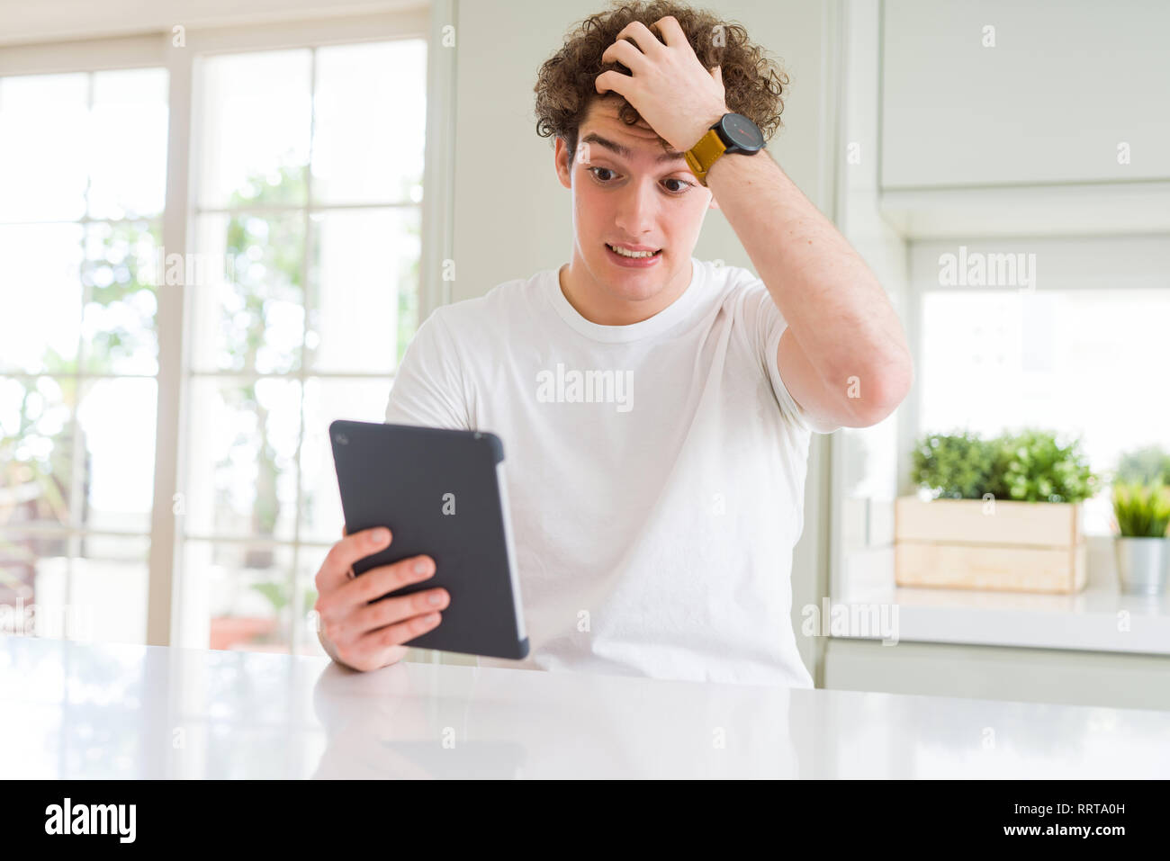 Young man using touchpad tablet stressed with hand on head, shocked ...