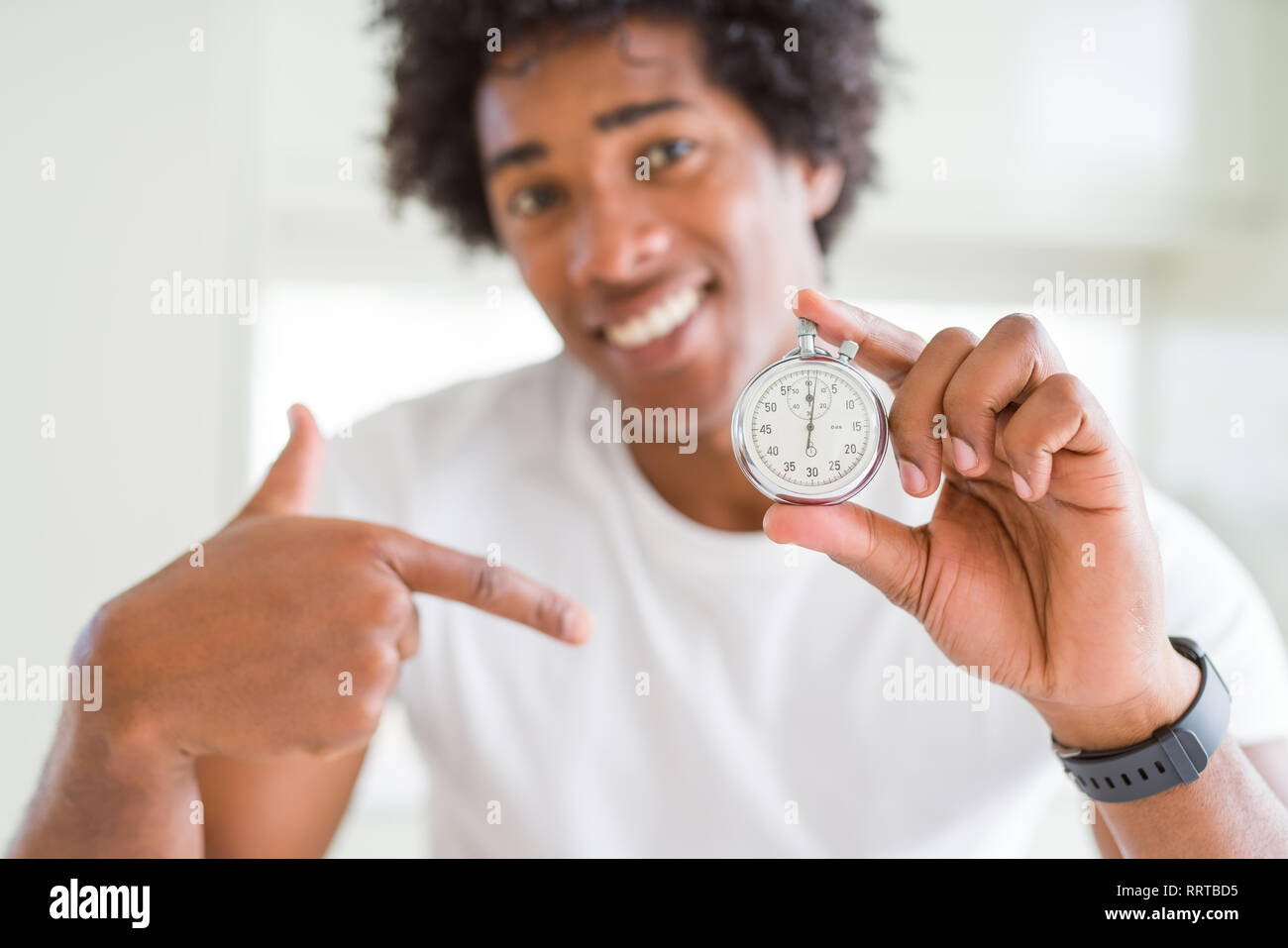 African American man holding stopwatch with surprise face pointing ...