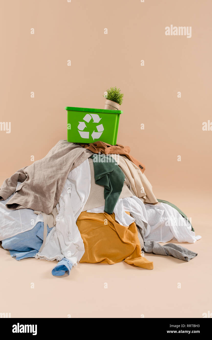 green recycling box with plant in pot on stack of clothing on beige ...