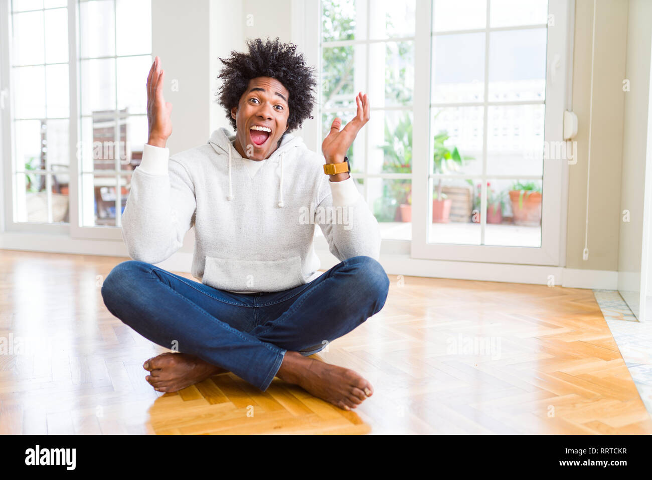 African American man sitting on the floor at home celebrating mad and ...