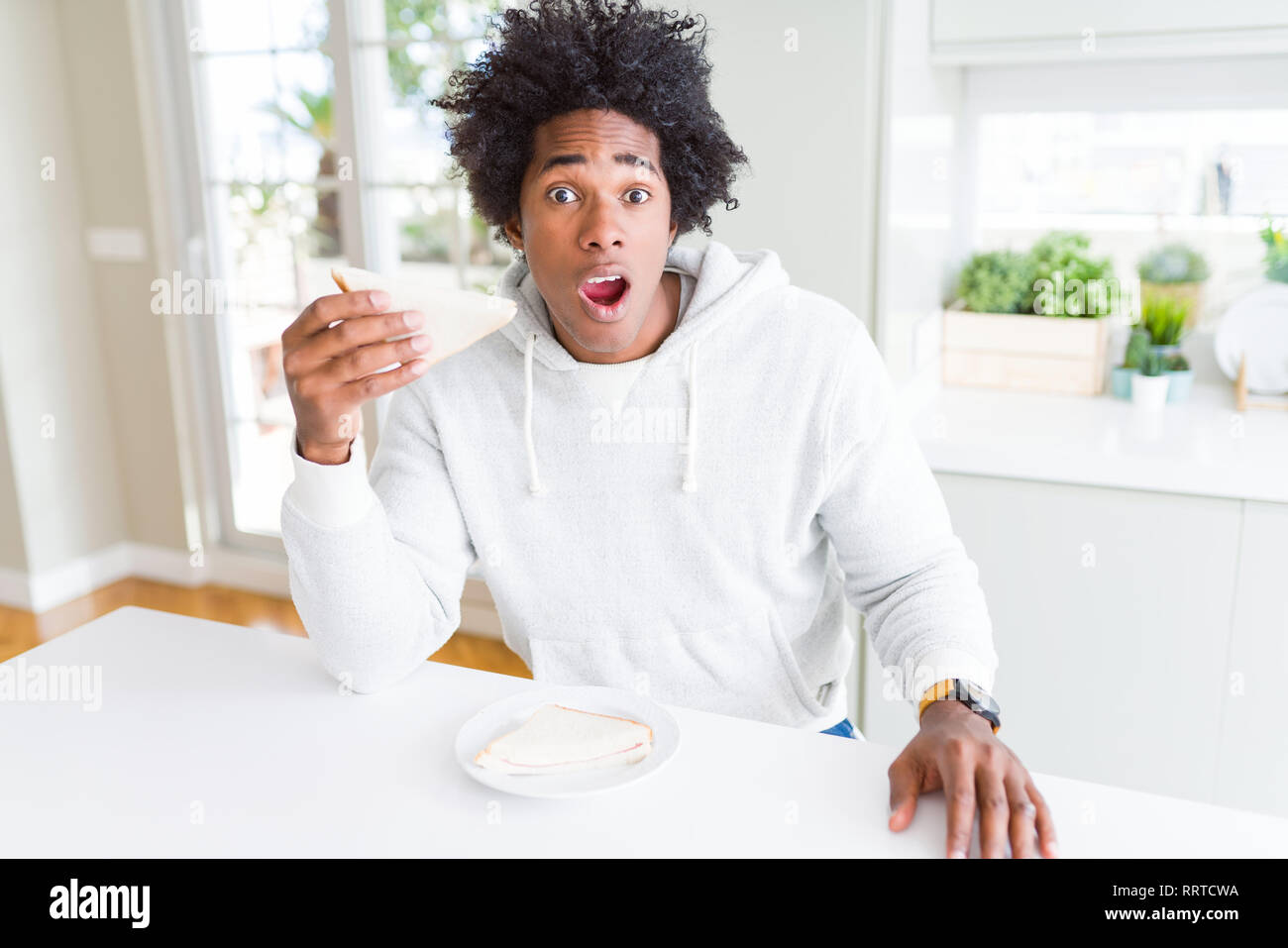 African American man eating handmade sandwich at home scared in shock ...