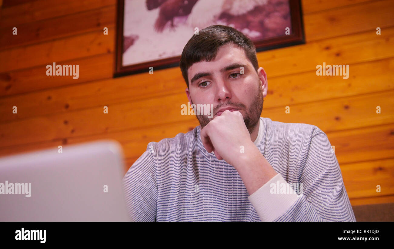 A puzzled man freelance worker sitting by the laptop and looking at the ...
