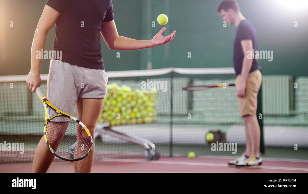Training on the tennis court. Young men hitting the ball from the floor ...