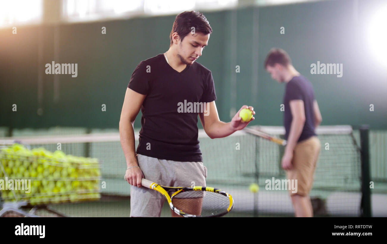 Training on the tennis court. Young men training. A man holding a ball ...