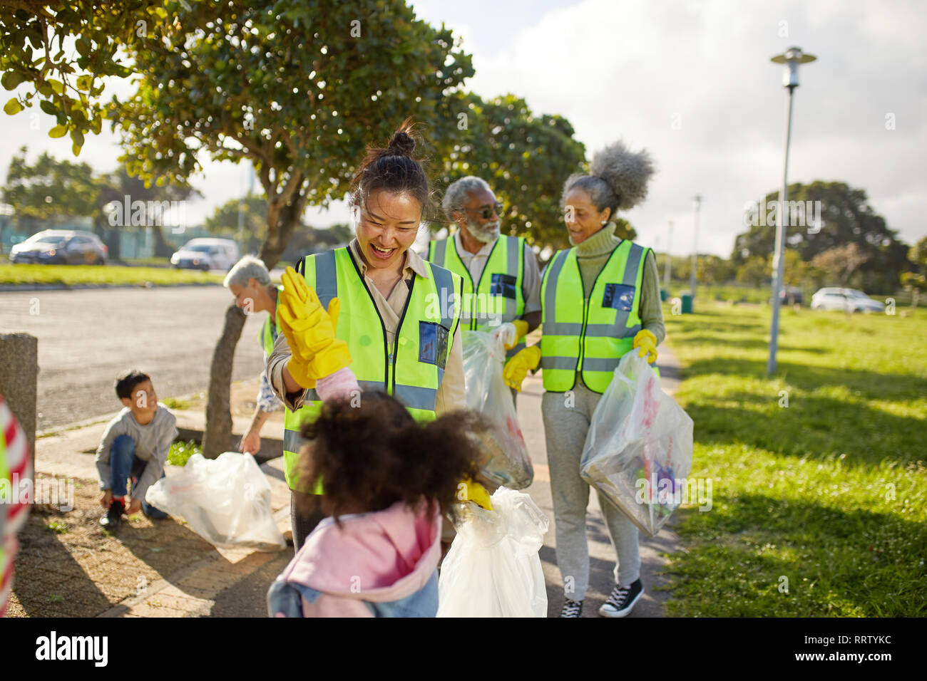 Happy volunteers high-fiving, cleaning up litter in sunny park Stock ...