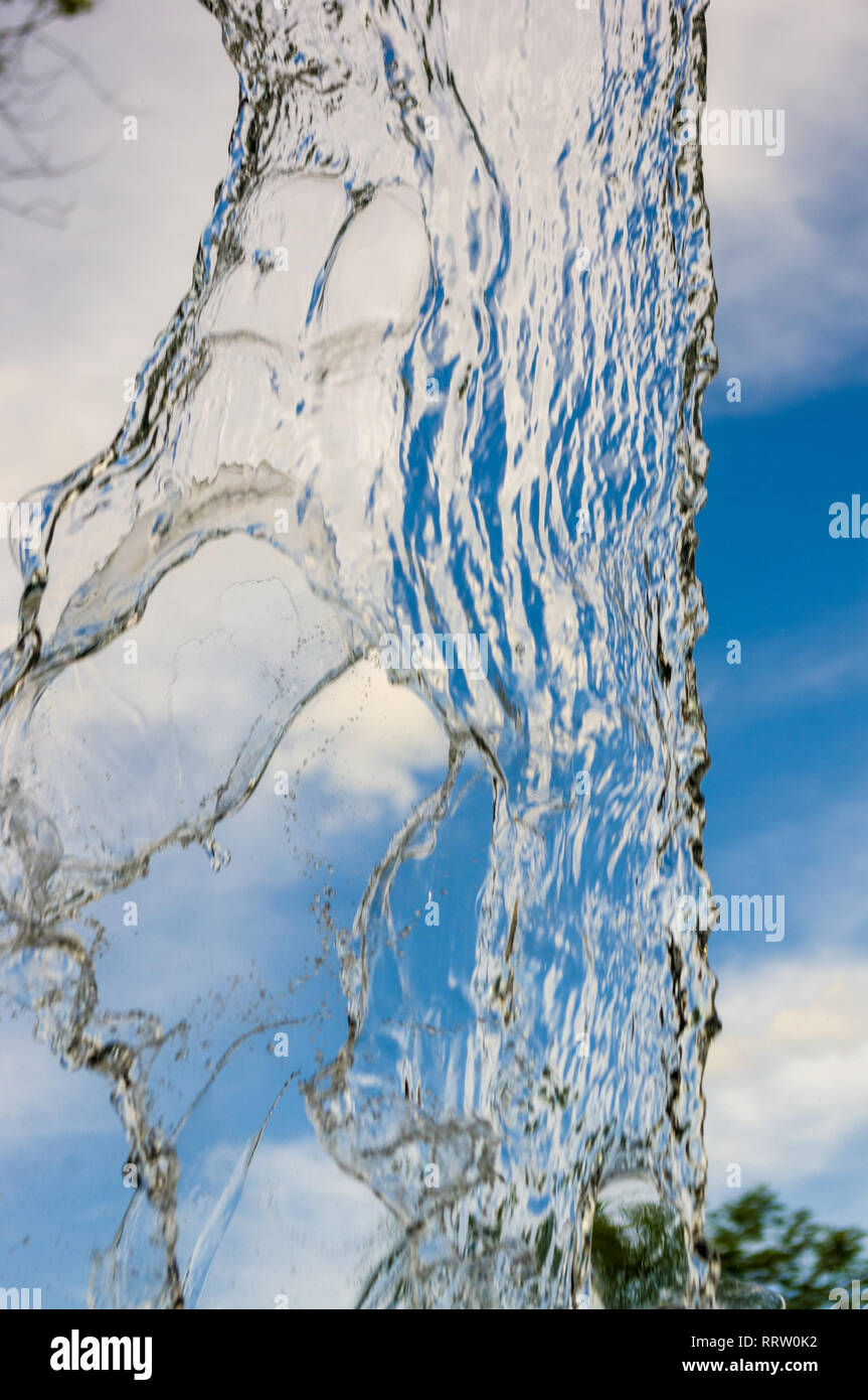 transparent falling water vertical flows against a blue sky and green ...