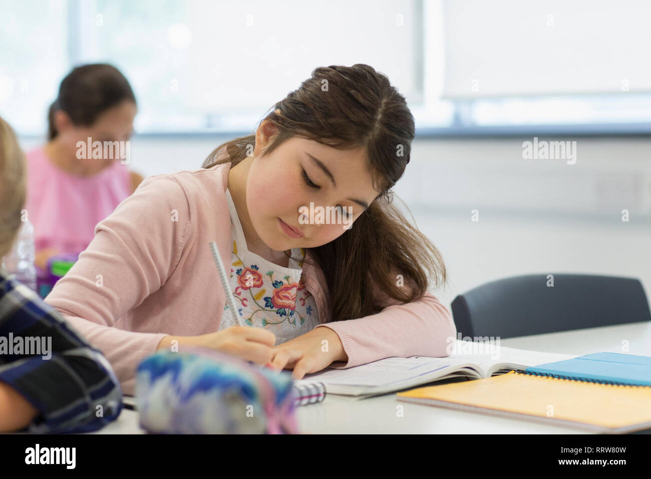 Focused junior high school girl student doing homework in classroom ...