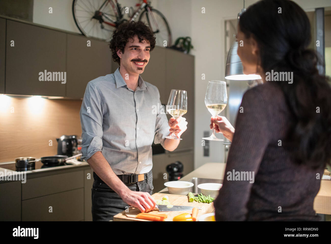 Couple preparing dinner and drinking white wine in apartment kitchen ...