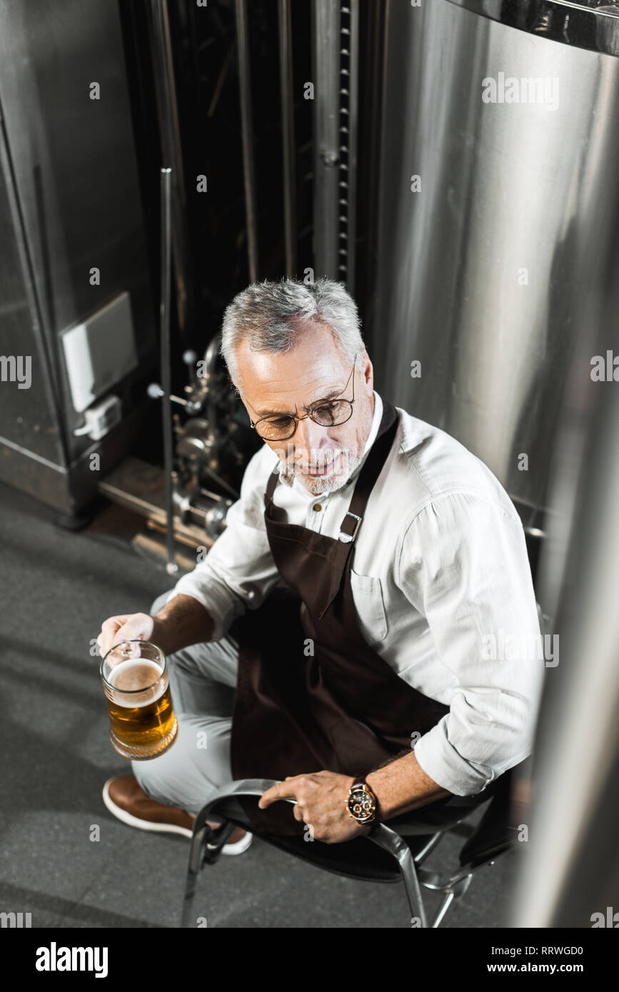 overhead view of handsome brewer in apron holding glass of beer in ...