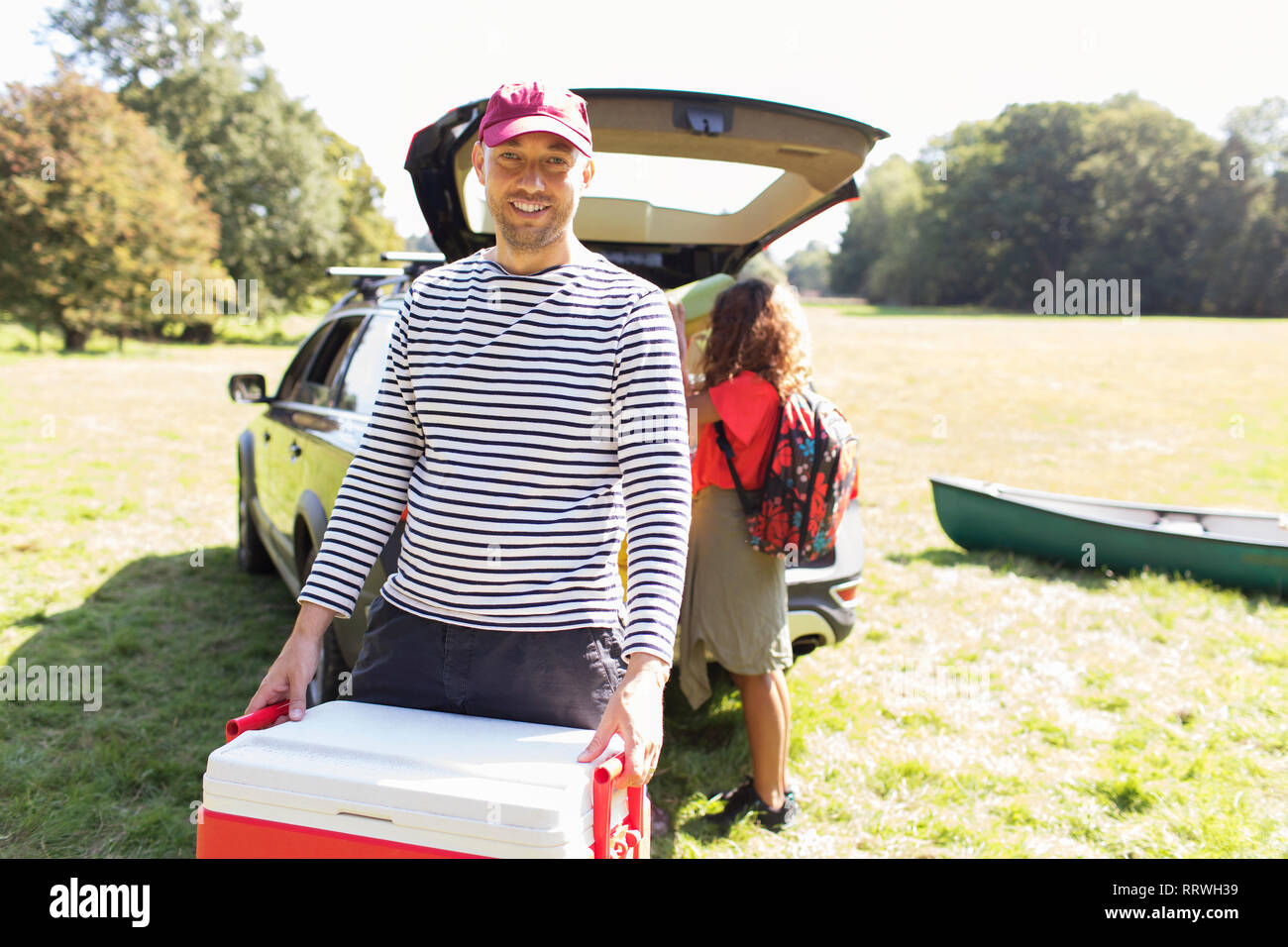 Portrait smiling man carrying camping cooler, unloading car in sunny ...