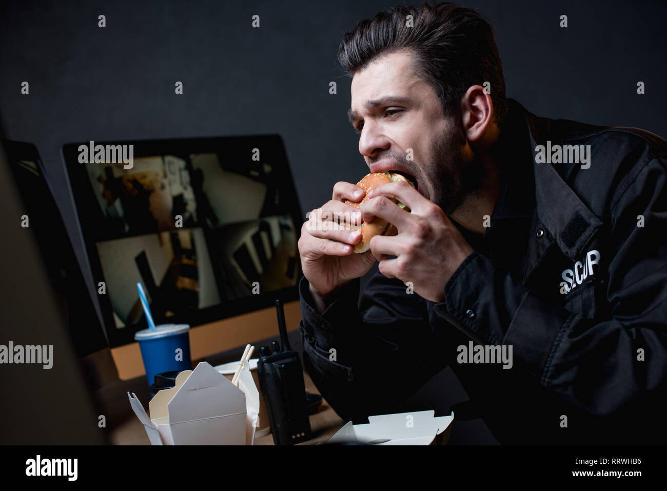 guard in uniform eating burger and looking at computer monitor Stock ...