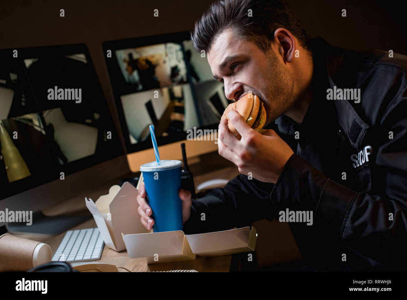 guard eating burger and holding paper cup at workplace Stock Photo - Alamy