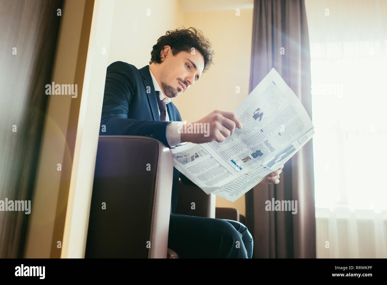 businessman in formal wear reading newspaper in hotel room with ...