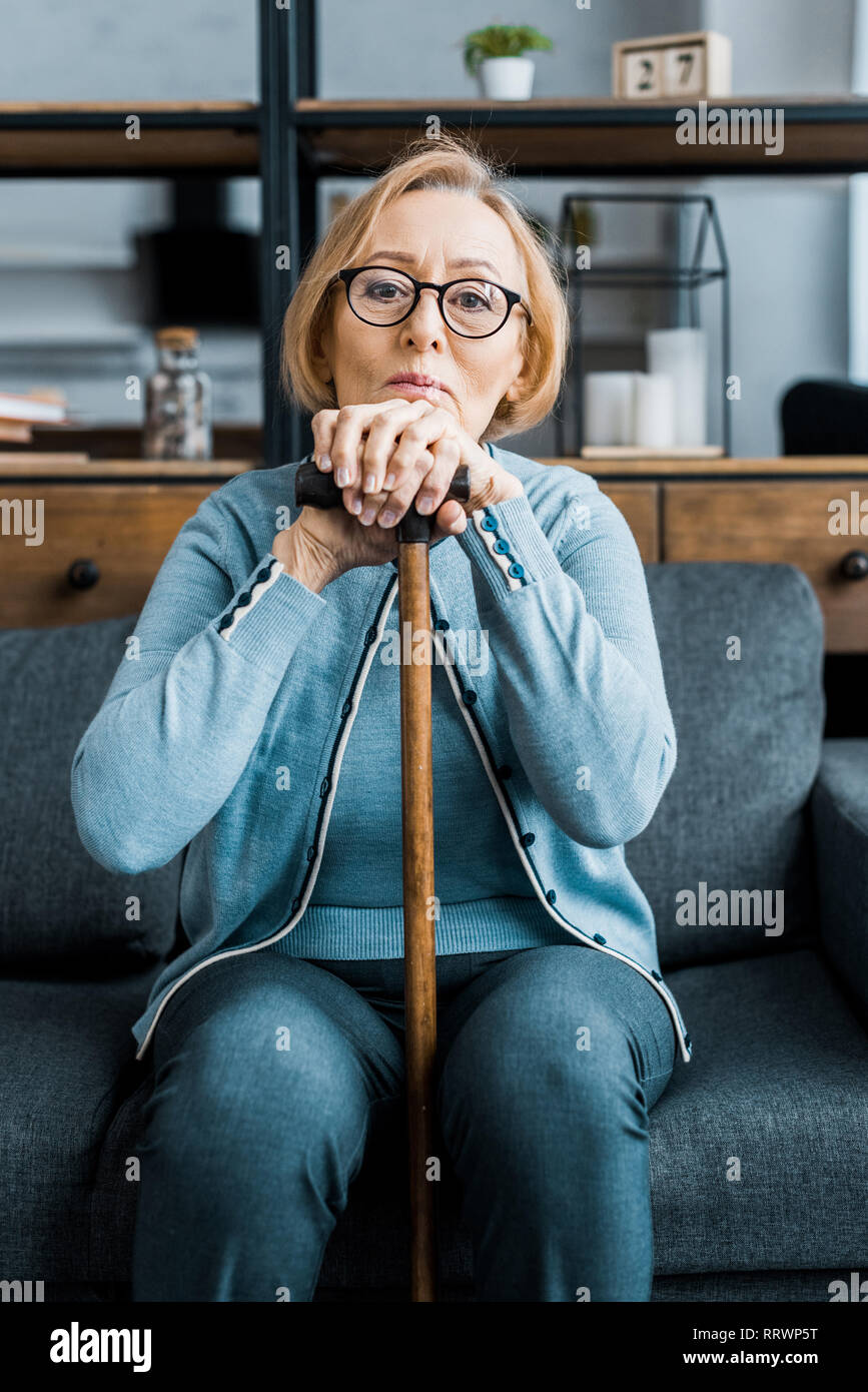Upset Senior Woman In Glasses Sitting On Couch Looking At Camera And