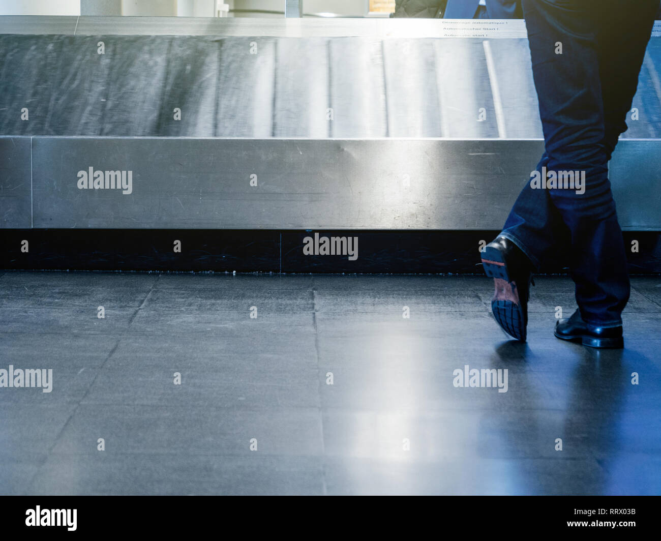 Rear view of a man with crossed legs waiting for luggage at the ...