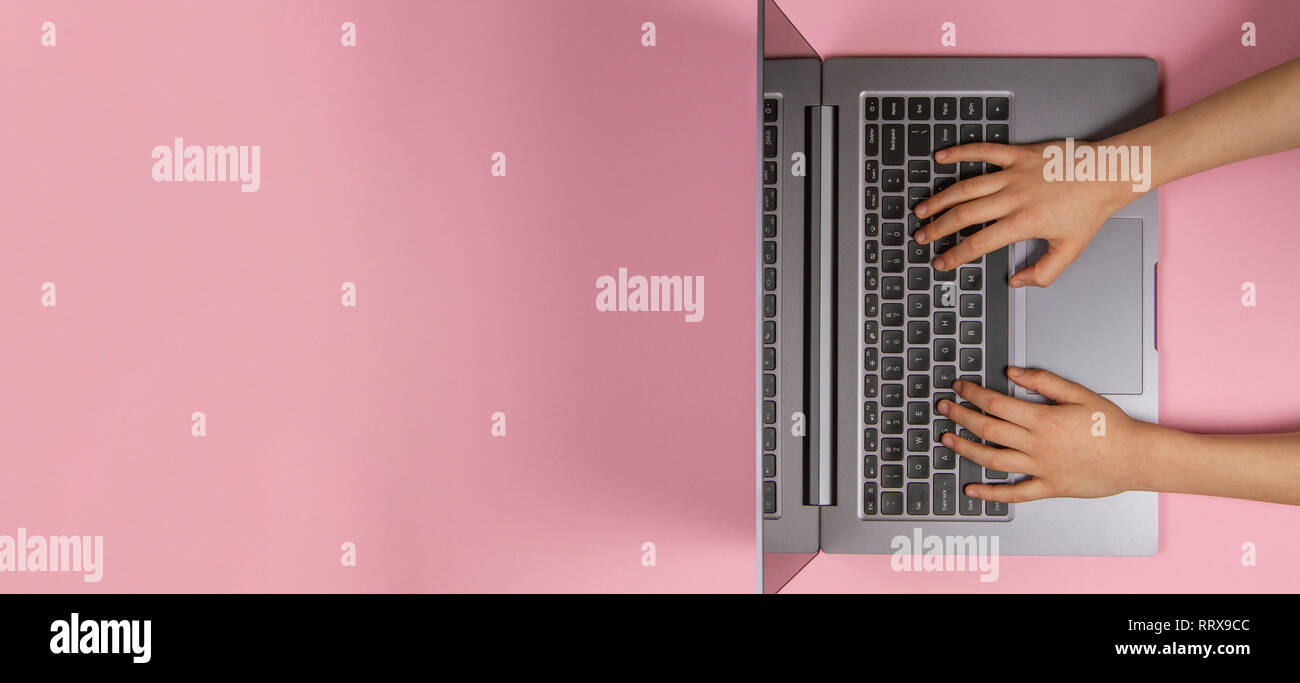 Kid hands typing on laptop computer keyboard, top view, pink banner ...