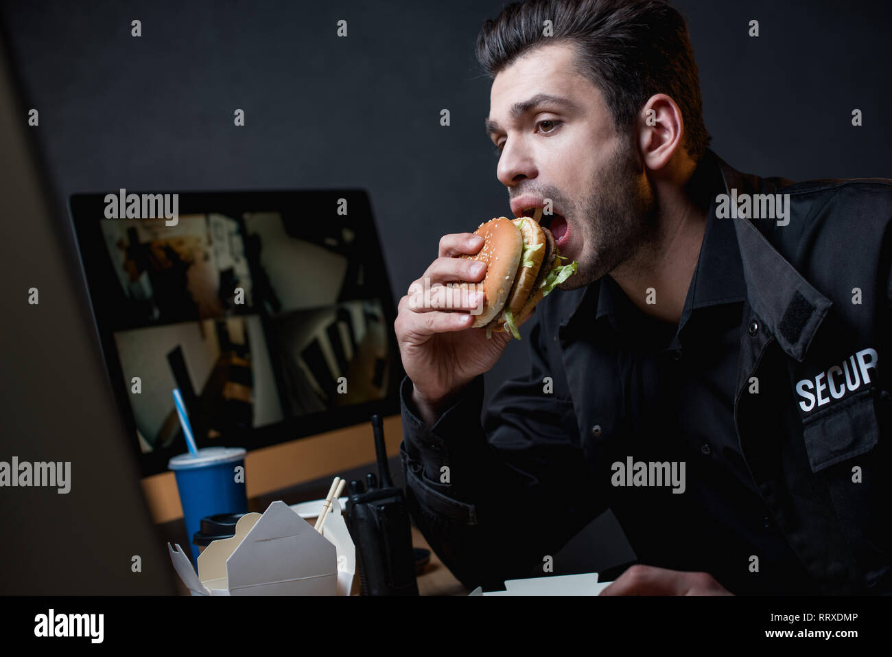 guard in uniform eating burger and looking at computer monitor Stock ...