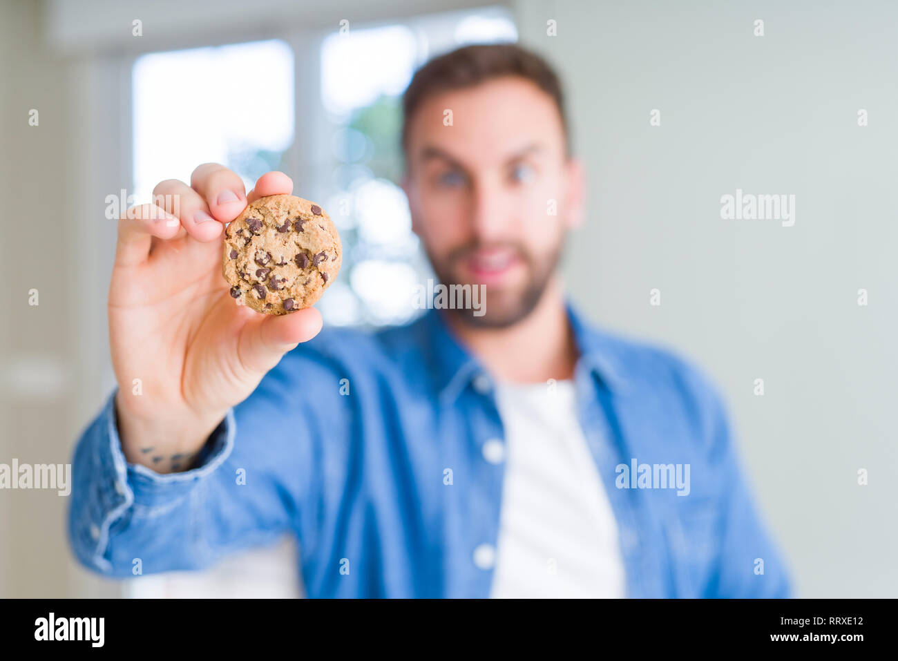 Handsome man eating chocolate chips cookies scared in shock with a ...