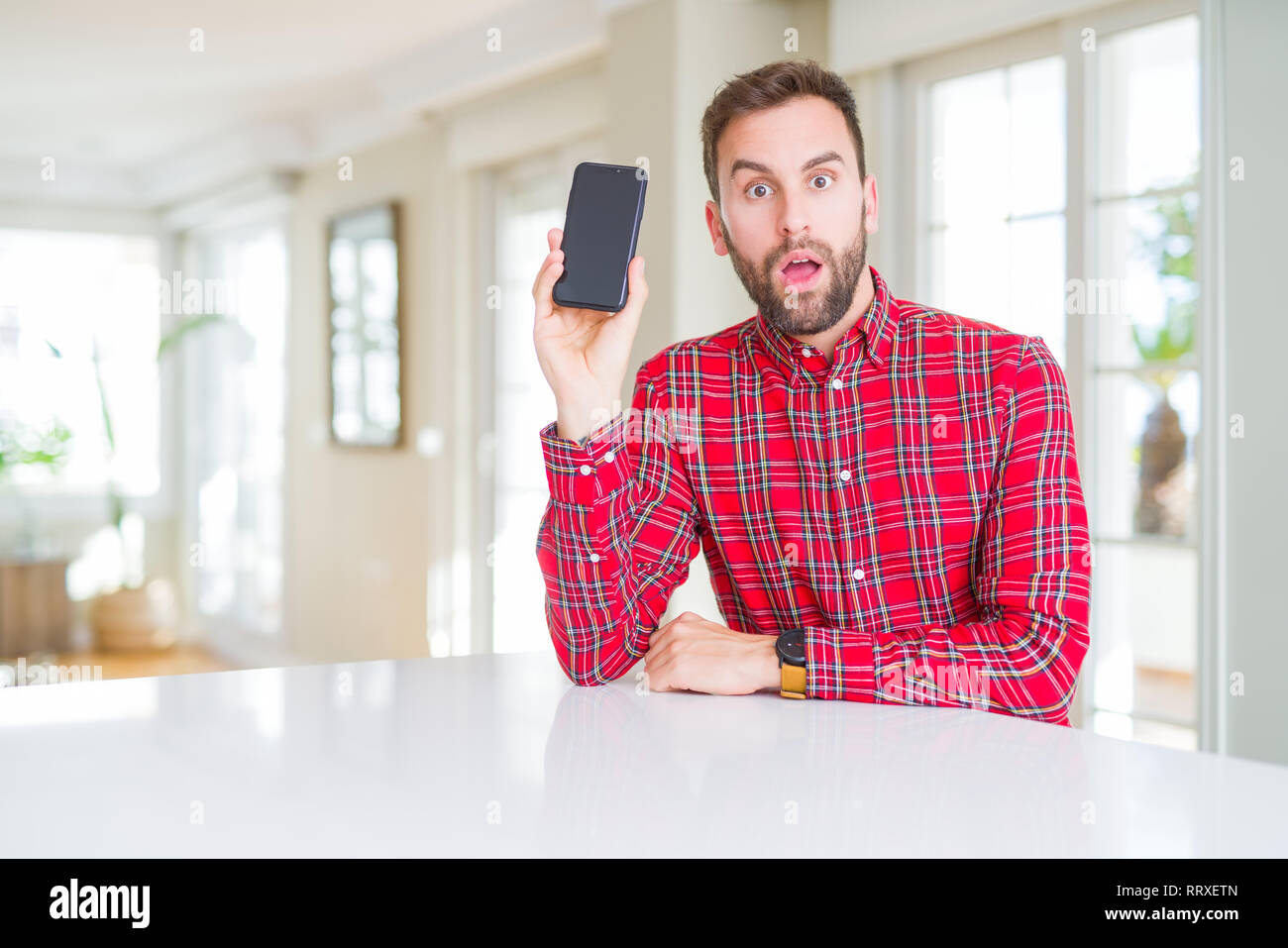 Handsome man showing smartphone screen scared in shock with a surprise ...