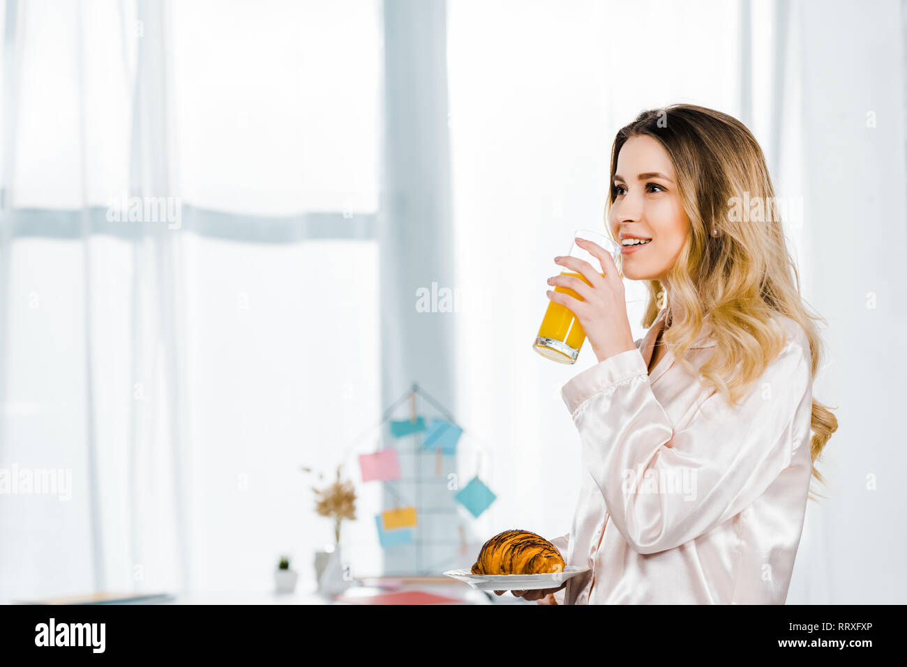 Inspired girl in pyjamas holding croissant and drinking orange juice in ...