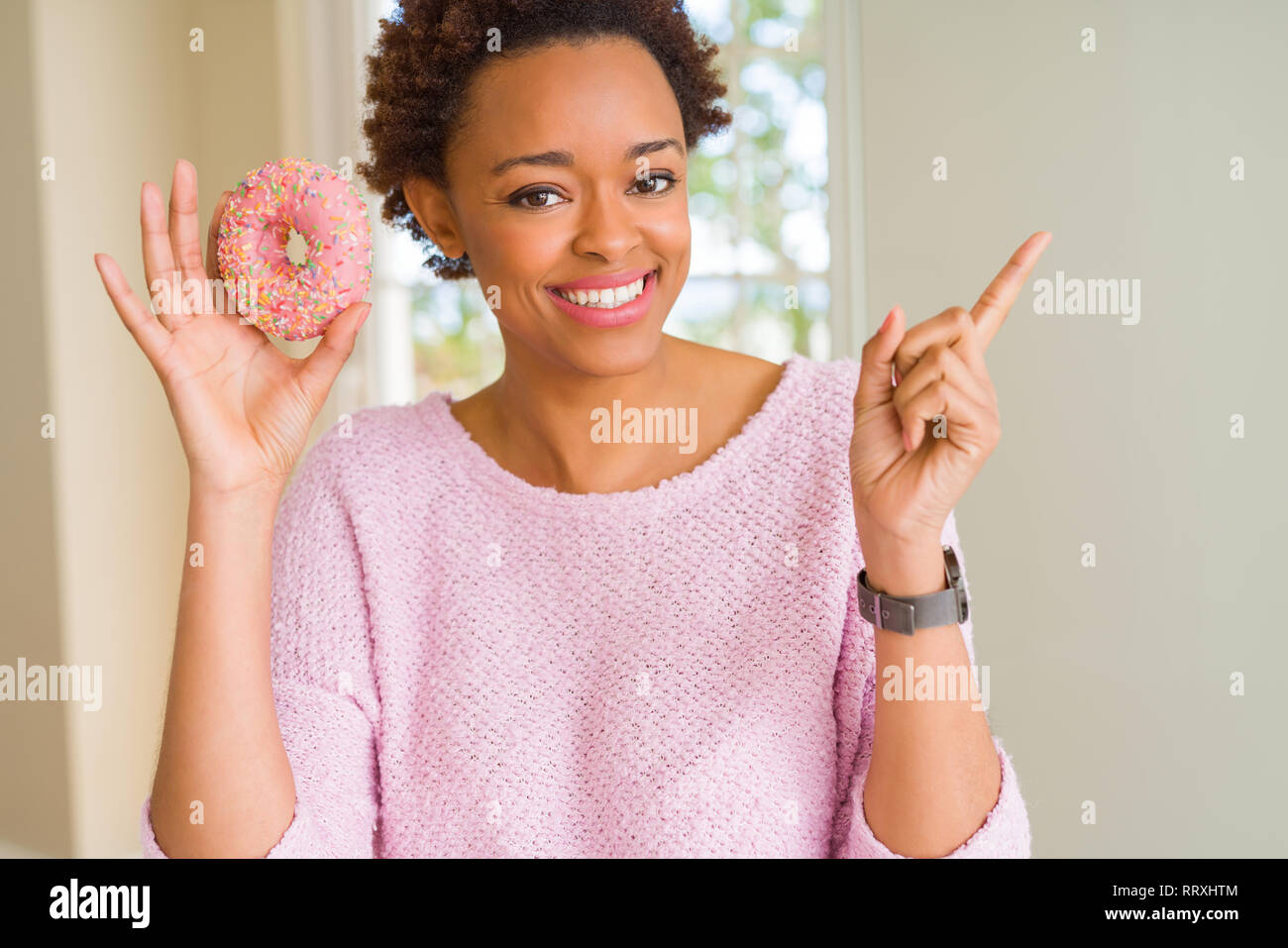 Young african american woman eating pink sugar donut very happy ...