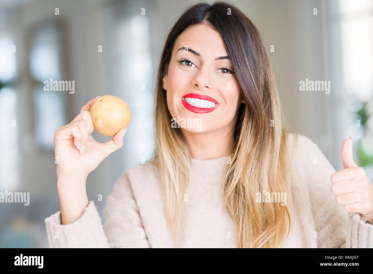 Young beautiful woman holding fresh potato at home happy with big smile ...