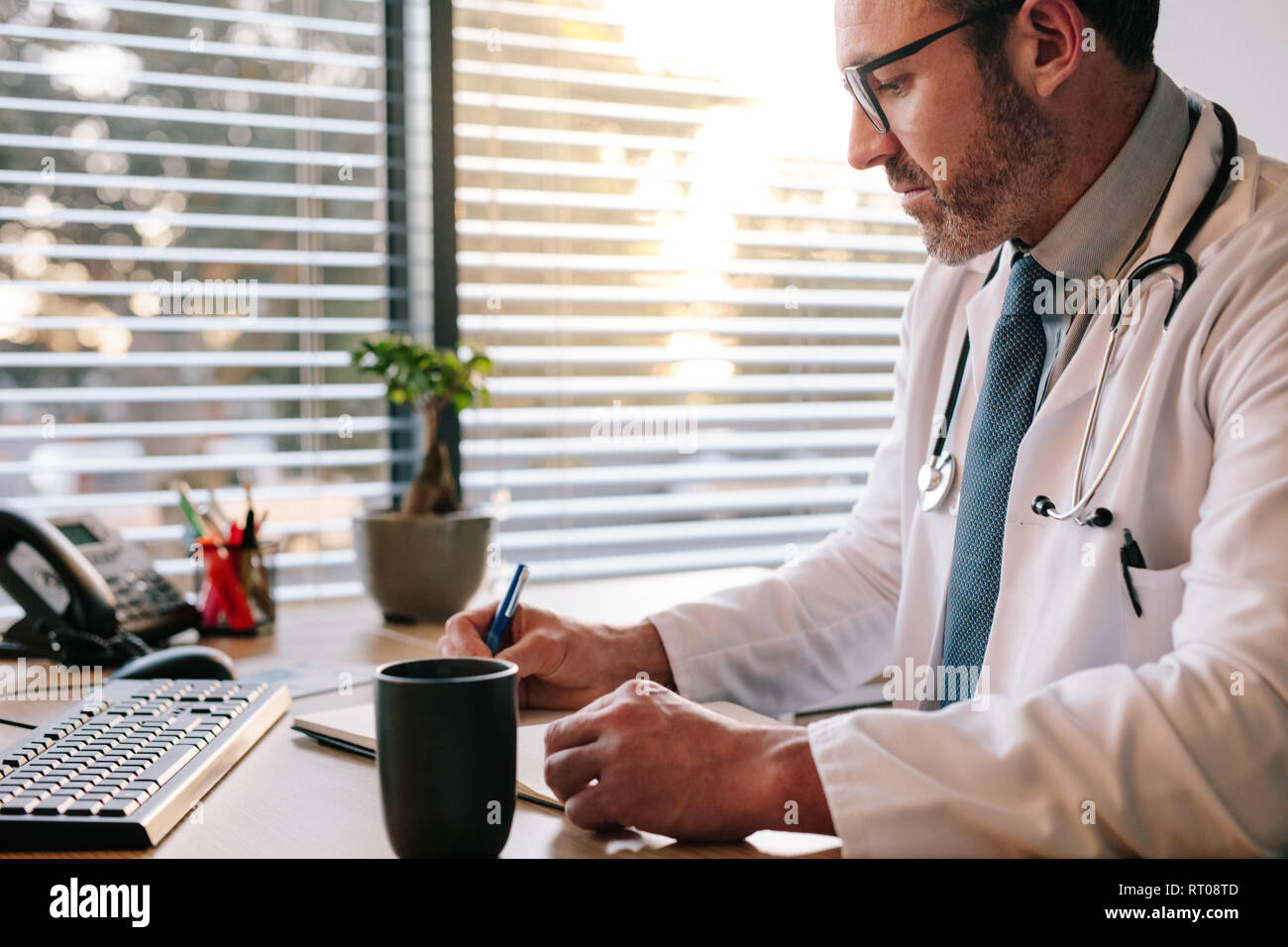 Mature male doctor making notes in his diary while sitting in his ...