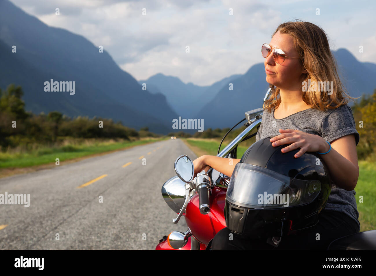 Woman riding a motorcycle on a scenic road surrounded by Canadian ...