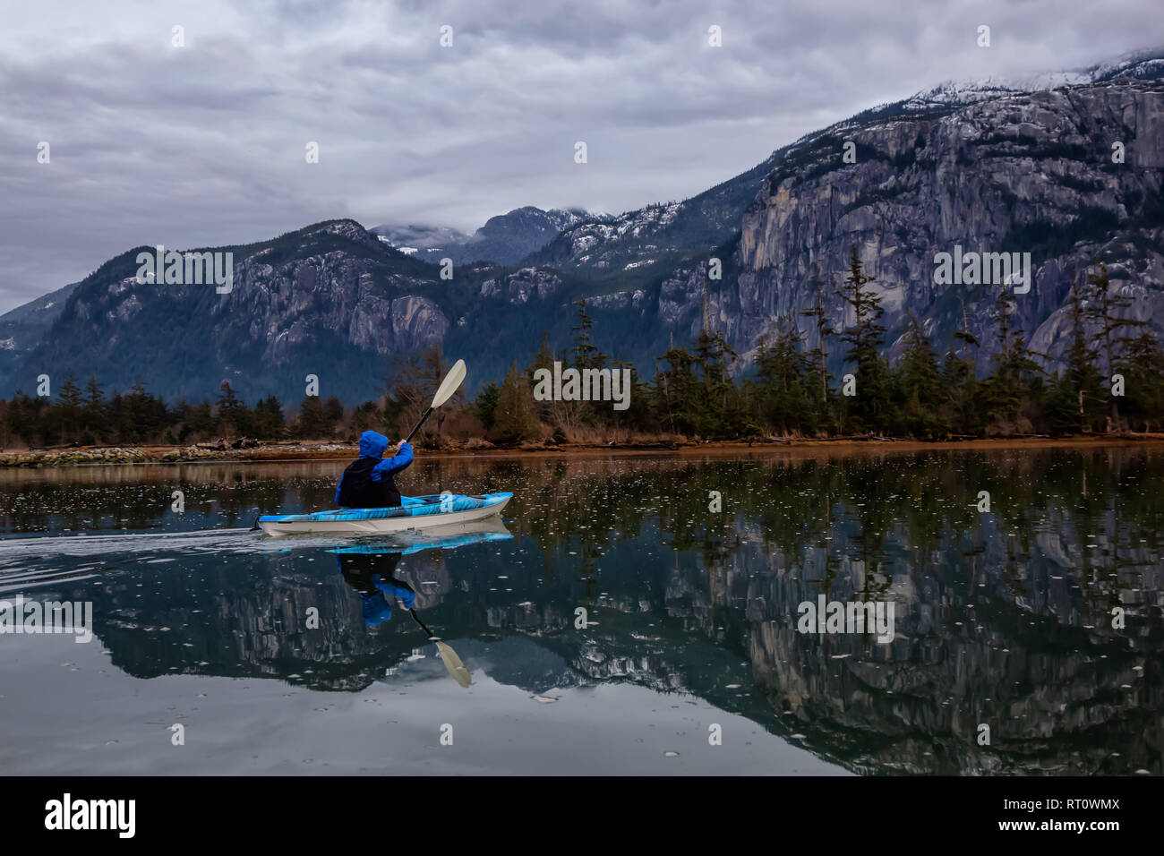 Adventurous man kayaking in peaceful water during a cloudy winter ...