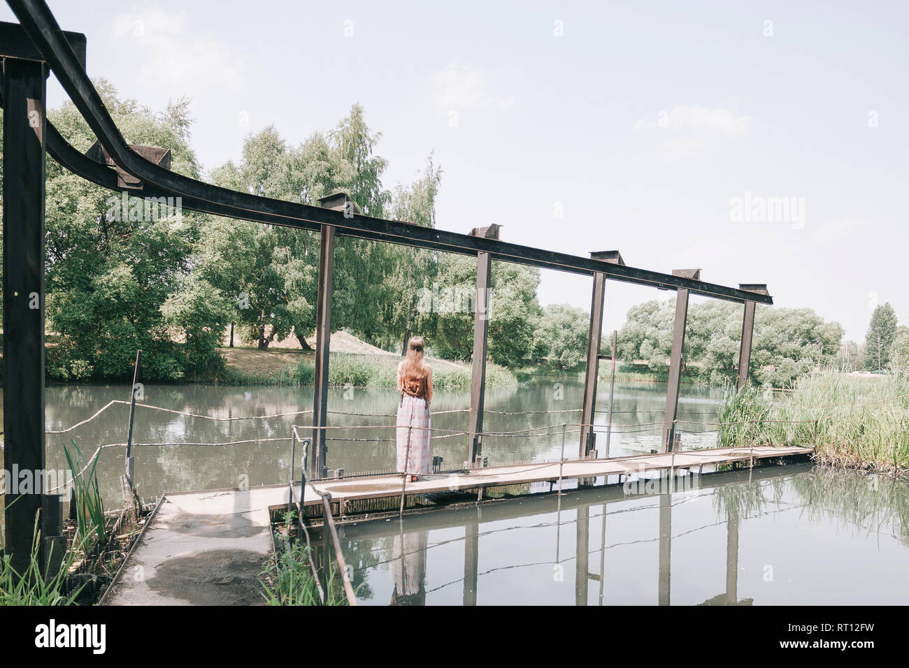 rear view. hippie girl walking on the bridge over the lake Stock Photo ...