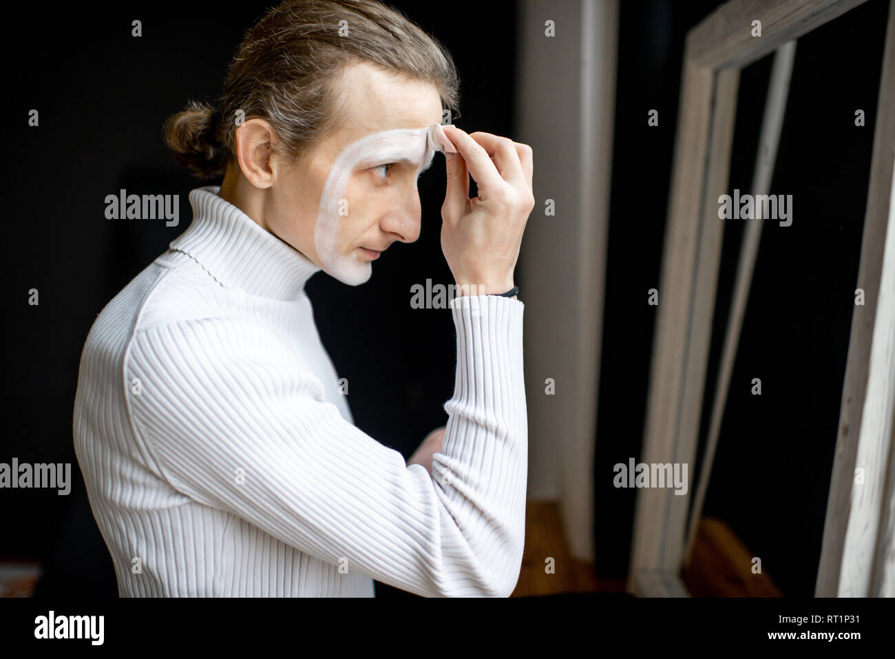 Actor putting mime makeup on his face preparing for perfomence indoors ...