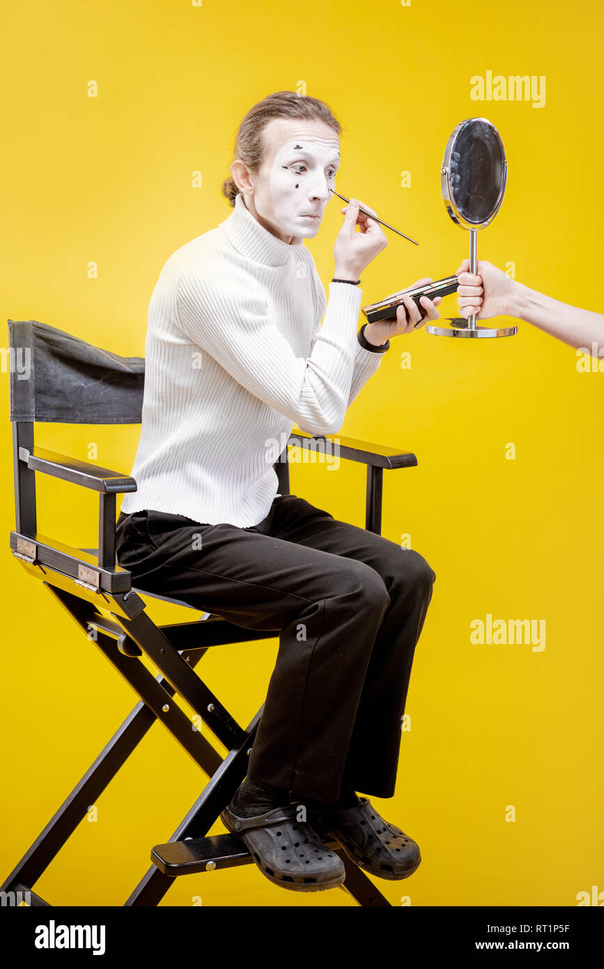 Actor applying facial makeup for pantomime performance sititng in the ...