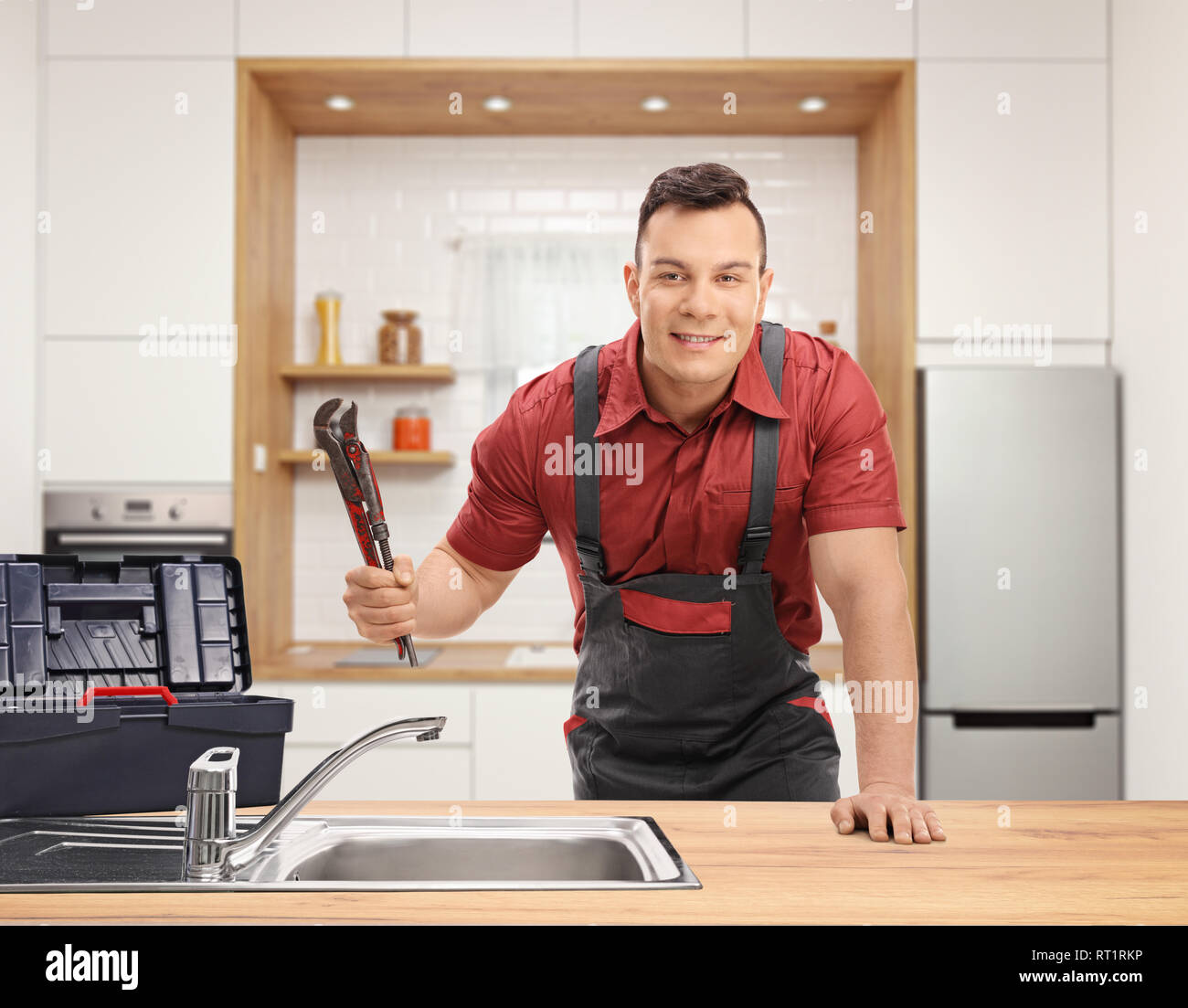 Plumber with a pipe wrench and a toolbox standing behind a sink in a ...