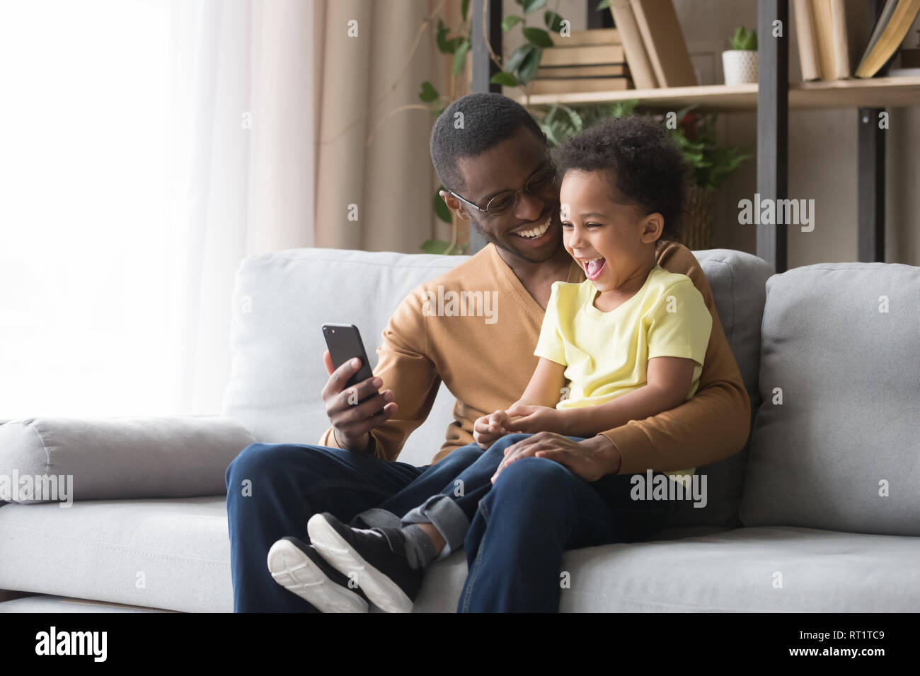 Happy african dad and toddler son laughing looking at cellphone Stock ...