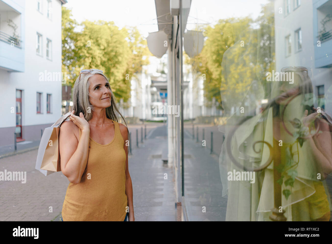 Portrait of smiling woman carrying shopping bags looking in shop window ...