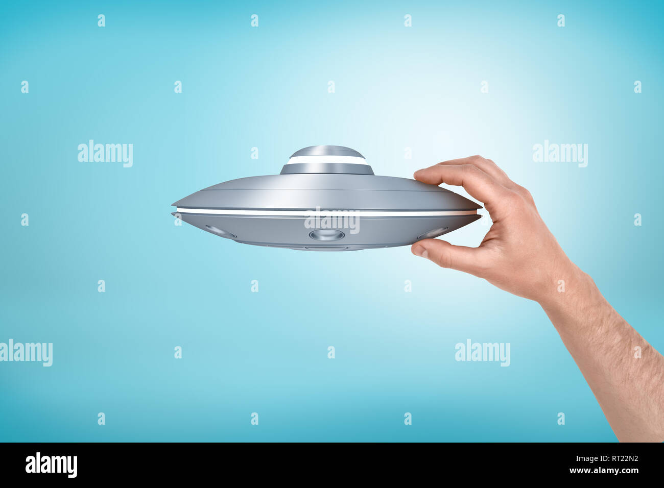 Close-up of man's hand holding small light-gray UFO on light-blue ...