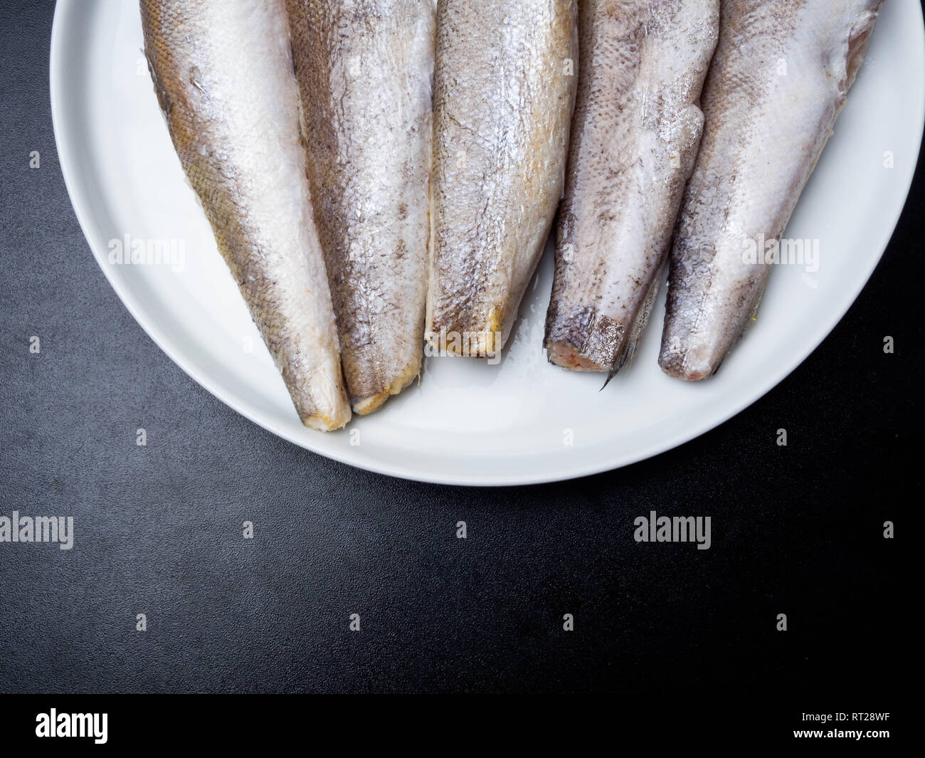 raw fish hake on white plate on black background Stock Photo - Alamy